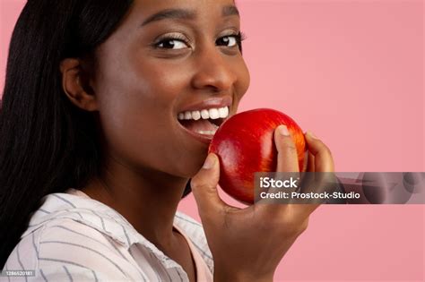 건강한 치아 개념 예쁜 흑인 여자 와 아름 다운 미소 물어 신선한 빨간 사과 에 핑크 스튜디오 배경 개념에 대한 스톡 사진 및