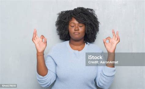 젊은 아프리카계 미국인 여자 겨울 스웨터를 입고 회색 그런 지 벽에 휴식과 명상 손가락으로 제스처를 하 고 폐쇄 눈으로 웃 고