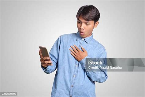파란 셔츠를 입은 충격받은 아시아 남자의 초상화가 휴대폰을 보고 있습니다 와우 얼굴 표정 흰색 배경에 고립된 이미지 20 24세에 대한 스톡 사진 및 기타 이미지 Istock