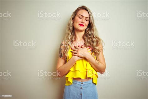 흰색 고립 된 배경 위에 서있는 노란색 티셔츠를 입은 젊은 아름다운 여성은 닫힌 눈과 얼굴에 감사하는 제스처로 가슴에 손을 미소를 짓고 있습니다 건강 개념 T 셔츠에 대한