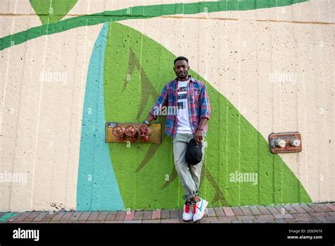 A Black Man Leans Against A Colorful Mural In An Urban Setting Stock