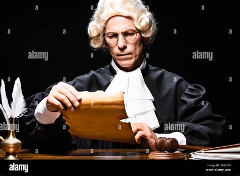 Judge In Judicial Robe And Wig Sitting At Table And Reading Document