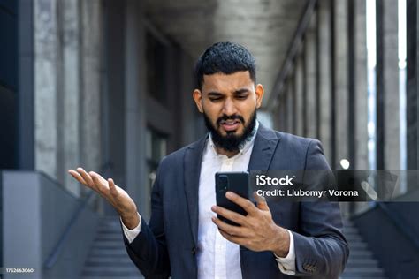 비즈니스 센터 근처 거리에 서서 전화를 들고 혼란스러워 보이는 양복을 입은 젊은 무슬림 사업가가 손을 벌리고 걱정했다 클로즈업