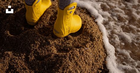회색 바지와 노란 장화를 신은 사람이 수역 근처의 갈색 모래 위에 서 있다 사진 Unsplash의 무료 사람의 이미지