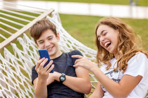 Пару молодых счастливых подростков Девушка и парень смеются и смотрят видео вместе на смартфоне