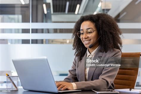 양복을 입고 책상에 앉아 사무실에서 노트북으로 작업하는 미소 짓는 젊은 아프리카계 미국인 비즈니스 여성 검사 보기에 대한 스톡 사진 및 기타 이미지 Istock