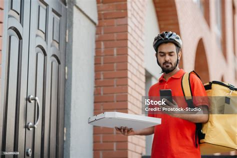 피자 배달 헬멧을 쓰고 있는 진지한 배달남자 배낭을 들고 상자를 들고 스마트폰을 바라보며 현관 문 근처 무선 기술에 대한 스톡 사진 및 기타 이미지 Istock