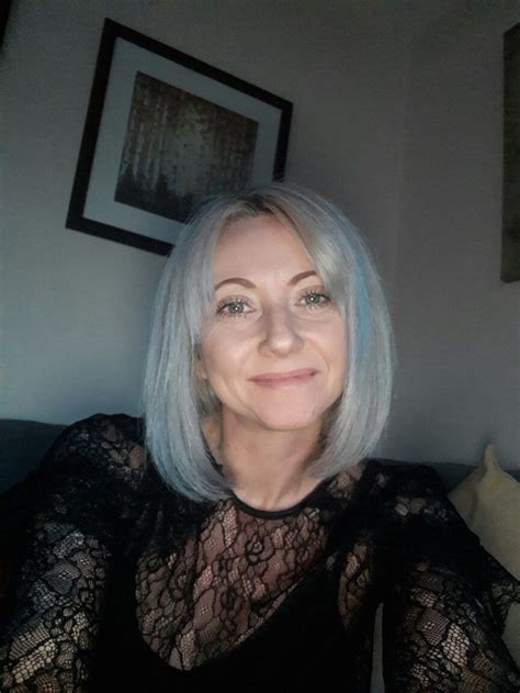An Older Woman With Grey Hair Wearing A Black Lace Top And Smiling At The Camera