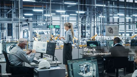 자동차 공장 사무실 컴퓨터를 사용하여 첨단 엔진을 위한 고급 3d 모델을 설계하는 자동차 엔지니어 팀 자동화된 로봇 암 산업용 조립 라인 제조 차량 초현대적에 대한 스톡