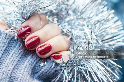 아름다운 광택 매니큐어와 회색 니트 스웨터에 여성의 손 부르고뉴 어두운 빨간색 체리 색상 손톱은 복사 공간과 실버 크리스마스 틴셀 화환의 배경에 손톱 갈란드 장식품에 대한