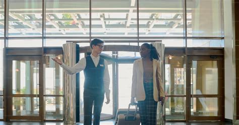 넓은 라운지를 따라 이동하는 동안 여행 가방을 들고 아프리카계 미국인 여행자를 만나는 고급 호텔의 젊은 우아한 주인 사진