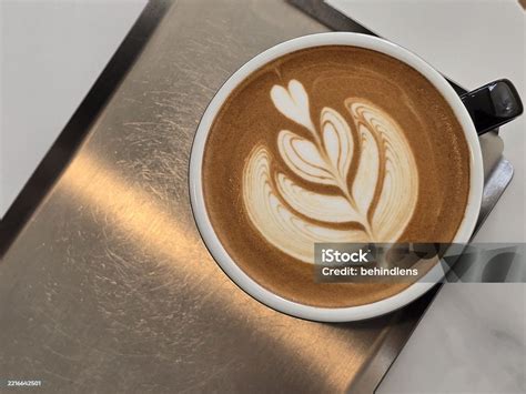 복잡한 폼 아트가 돋보이는 아름답게 제작된 라떼는 금속 표면의 블랙 컵에 담겨 음료에 예술적 터치를 더하는 하트와 나뭇잎 디자인을 선보입니다 0명에 대한 스톡 사진 및 기타