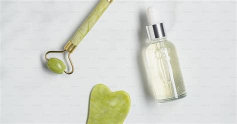 천연 노화 방지 옥 돌 에센셜 오일 스포이드 병 및 대리석 테이블에 녹색 잎이 있는 옥 롤러 얼굴 피부 관리 개념입니다