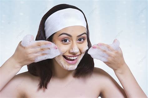 Portrait Of Beautiful Woman Applying Soap On Face Against Blue