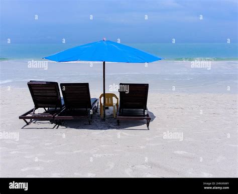 Three Sunbeds And A Blue Umbrella On The Beach With White Sand On The