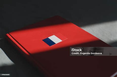 표지에 프랑스 국기가 있는 빨간 교과서가 밝은 천 표면 위에 놓여 있고 부분적으로 그림자로 덮여 있습니다 언어 학습 교육 프랑스 국가 정체성의 개념 개념에 대한 스톡 사진
