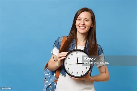 T셔츠에 젊은 캐주얼 웃는 매력적인 여자 학생의 초상화 배낭 데님 옷 잡아 파란색 배경에 고립 된 알람 시계 고등학교에서 교육입니다 광고에 대 한 공간을 복사 합니다 20