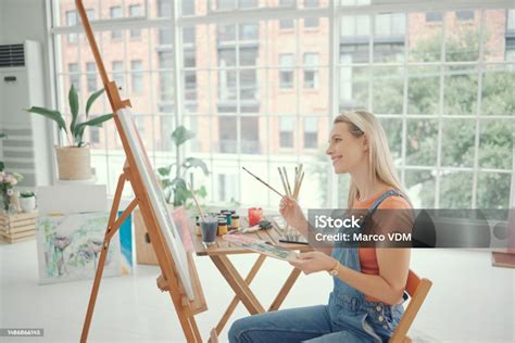 이젤과 수채화를 사용하여 캔버스에 그림을 그리는 스튜디오나 작업장에서 여성과 함께 그림을 그리고 예술을 하고 행복합니다 유채화