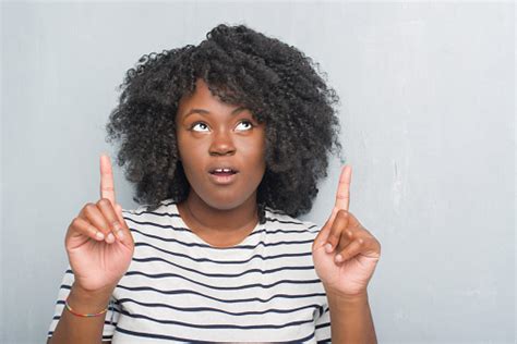 젊은 아프리카계 미국인 플러스 크기 여자 회색 그런 지에 깜짝 놀라게 하 고 놀 보고 하 고 손가락으로 가리키는 벽 하 고 무기를 제기 T 셔츠에 대한 스톡 사진 및 기타