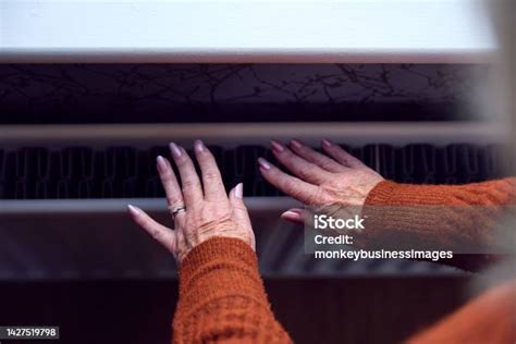 생활 에너지 위기의 비용으로 집에서 라디에이터로 따뜻하게 유지하려는 노인 여성의 클로즈업 기체 물리 구조에 대한 스톡 사진 및