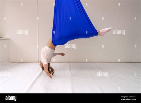 A Young Woman Poses While Doing Anti Gravity Aerial Yoga In A Blue