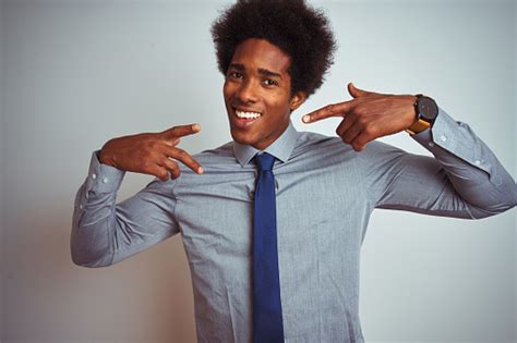 아프로 머리를 입고 셔츠를 입고 고립 된 흰색 배경에 넥타이를 매고 손가락 이빨과 입으로 가리키는 쾌활한 미소를 짓고 있습니다