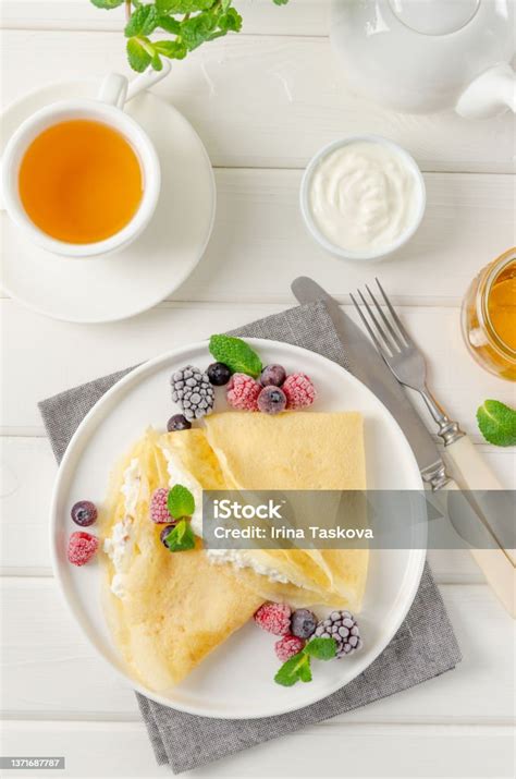 전통적인 얇은 팬케이크 또는 크레페와 코티지 치즈 건포도 열매 꿀 사워 크림이 흰색 나무 배경에 있습니다 마레그나에 대한 음식