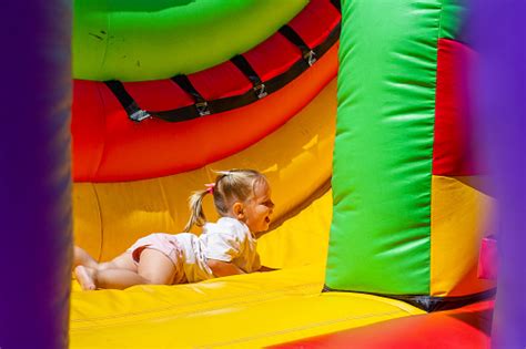 미소 짓고 웃으면서 어린 소녀는 풍선 멀티 컬러 트램폴린 슬라이드를 미끄러 져 내려갑니다 아이는 화창한 더운 날에 여름 공원에서 즐거운 시간을 보냅니다 놀이 공원에서