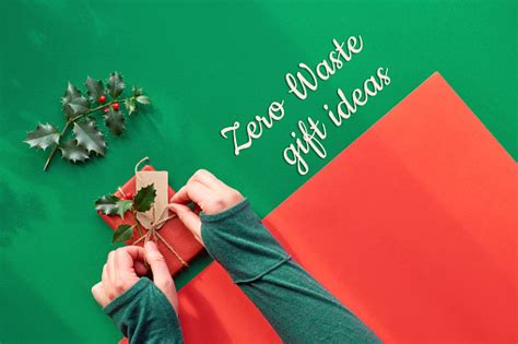 창조적 인 파노라마 플랫긴 그림자와 녹색과 빨간색 종이에 누워 홀리 장식 된 여성 손 홀디 포장 선물 상자 환경 친화적 인 Xmas 텍스트 제로 폐기물 선물 아이디어 12