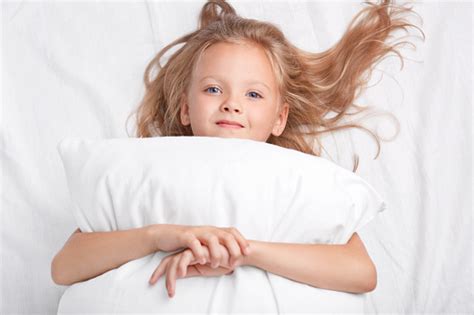 꿈꾸는 블루 빛 머리를 가진 여자 아이 외 눈 박이 베개를 포용 긍정적으로 카메라 화이트 침대 좋은 분위기에서 건강 한 수 면 후에 포즈 어린이 침구와 휴식 개념 귀여운에