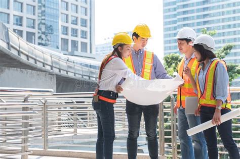 Group Of Asian Engineers In Helmets Looking At A Blueprint To Discuss And Plan For Build A