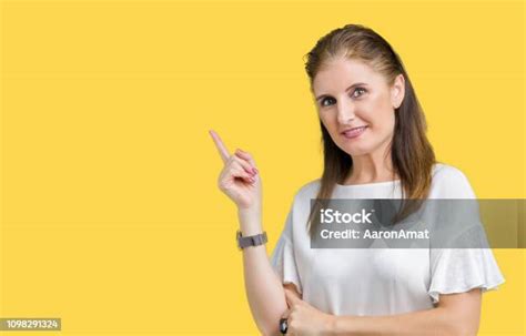 중간 나이 성숙한 아름 다운 여자 얼굴에 큰 미소와 함께 고립 된 배경 위에 카메라를 보고 옆에 손 및 손가락으로 가리키는 가리키기에 대한 스톡 사진 및 기타 이미지