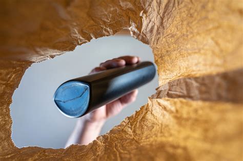 한 손이 종이 봉투에서 검은 색 플라스틱 병을 가져옵니다 성숙한 남자의 손은 오픈 브라운 백 위에 샴푸 병을 들고 있습니다 아래에서 위로 촬영합니다 닫습니다 선택적 초점