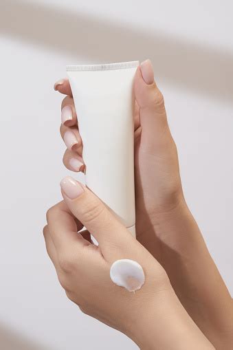 적용된 핸드 크림과 크림의 흰색 튜브의 모형을 가진 여자의 손 흰색 배경에 햇빛에 화장품에 대한 라벨이 붙지 않은 포장 스킨케어의 개념 짙은 그림자 깨끗한에 대한 스톡 사진
