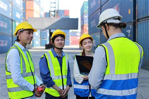 보호복을 입은 다민족 기술자 엔지니어와 사업가 그룹이 컨테이너 화물 현장에서 컴퓨터와 함께 토론하고 연구하고 브레인스토밍하고