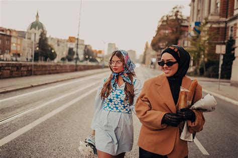 현대 유럽 여성과 히잡을 쓴 무슬림 여성이 신문 꽃 빵을 손에 들고 19세기 옷을 입고 도시의 거리를 걷고 있습니다 18 19세에 대한 스톡 사진 및 기타 이미지 Istock