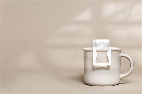 큰 컵에 분쇄 커피와 드립 커피 가방 햇빛베이지 배경에 양조를위한 종이 가방 드립 커피 필터 패키지 복사 공간이있는 사이드 뷰 흑백 파스텔 컬러 가루로 빻은에 대한 스톡