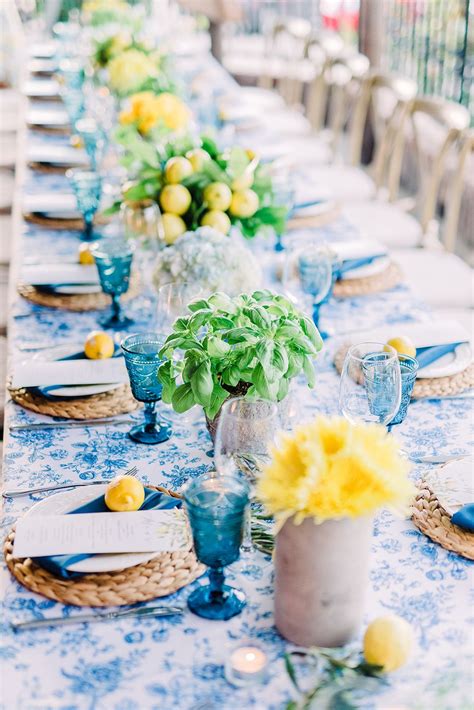 A Long Table Is Set With Blue And Yellow Place Settings Lemons In Vases