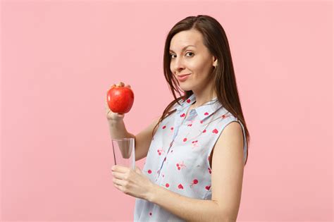 신선한 잘 익은 빨간 사과 과일 스튜디오에서 분홍색 파스텔 벽 배경에 고립 된 유리 컵을 들고 여름 옷에 예쁜 젊은 여자 사람들은 생생한 라이프 스타일 휴식 휴가 개념입니다