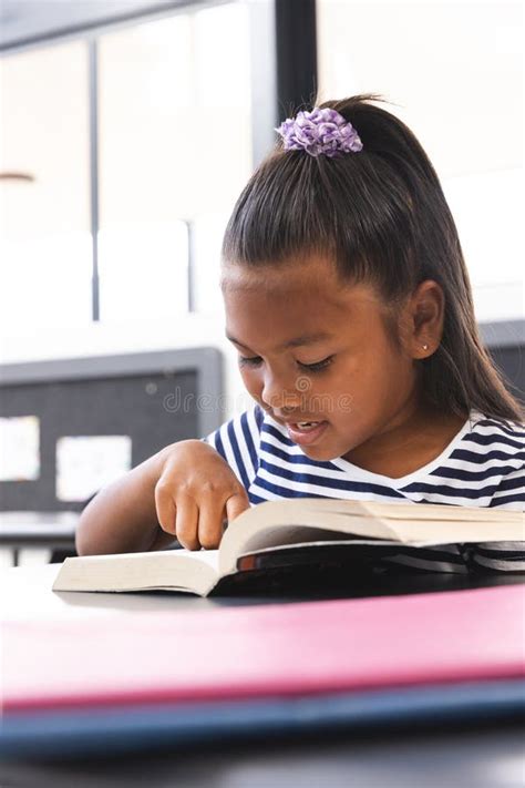 In School Young Biracial Girl Focusing On Reading A Book In The