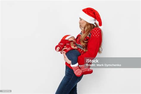 흰색 배경에 서있는 산타 의상을 입은 어린 아기와 함께 산타 모자를 쓴 젊은 어머니 12월에 대한 스톡 사진 및 기타 이미지 12월 가족 겨울 Istock