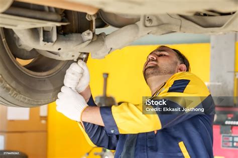 노란색 유니폼과 장갑을 착용하고 자동차 작업장에서 자동차 아래에서 일하는 정비사는 차량 수리에 중점을 두고 전문 지식과 유지 보수 작업의 세부 사항에 대한 관심을 보여줍니다