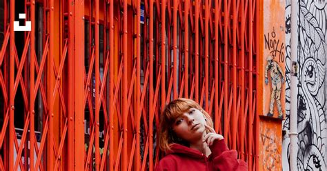 흰색과 검은색 꽃무늬 벽에 기대어 있는 빨간 긴팔 셔츠를 입은 여자 사진 Unsplash의 무료 런던 이미지