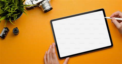 카메라와 화분이 있는 세련된 작업 공간에서 디지털 태블릿을 사용하는 스타일러스 펜을 가진 여성 손의 상위 뷰 클리핑 경로 사진