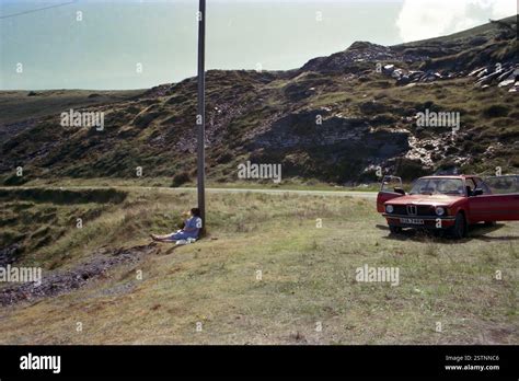 Girl Sitting Against A Telegraph Pole Adjacent To A Red Bmw 320 Car In