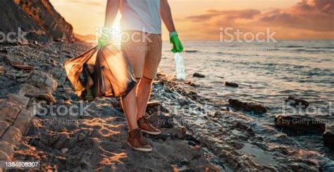 한 남성 자원봉사자가 쓰레기로 폴레틸렌 가방 두 개를 들고 있다 배경에 바다와 일몰 복사 공간이 있는 배너입니다 환경 보호 및 해안 정화의 개념 제로 웨이스트에 대한 스톡