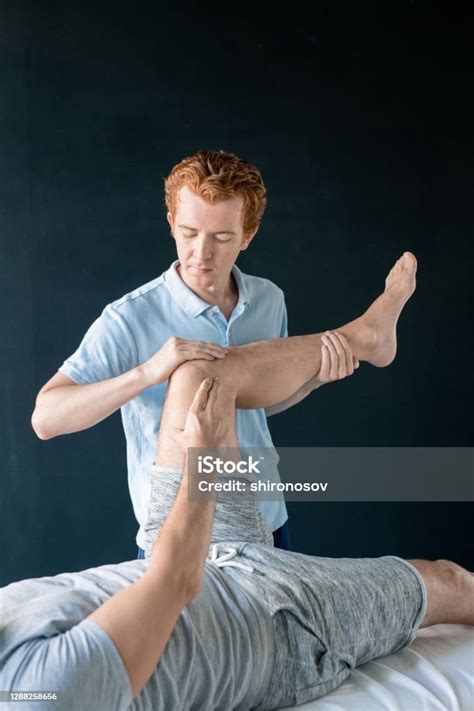 Contemporary Clinician Holding Leg Bent In Knee Of His Patient Lying On