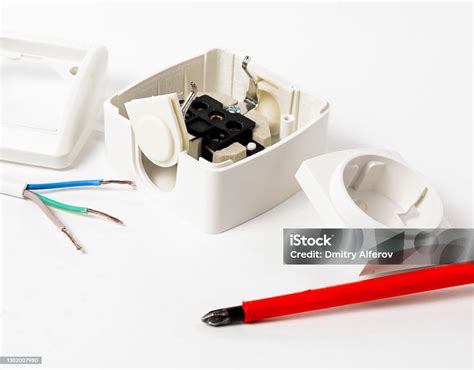 흰색 테이블에는 설치할 준비가 된 분해된 전기 콘센트 제거된 전선 및 전기 기술자를 위한 빨간색 드라이버가 있습니다 전기 설치