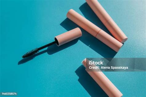 마스카라 용 핑크 클린 메이크업 브러시는 열린 튜브 닫힌 화장품 튜브 립글로스 액체 립스틱 그림자가있는 파란색 배경에 분홍색 아이 라이너 옆에 있습니다 복사 공간 0명에