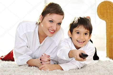 Mom With Son Lying On Floor And Watching Tv Using Remote Control Stock